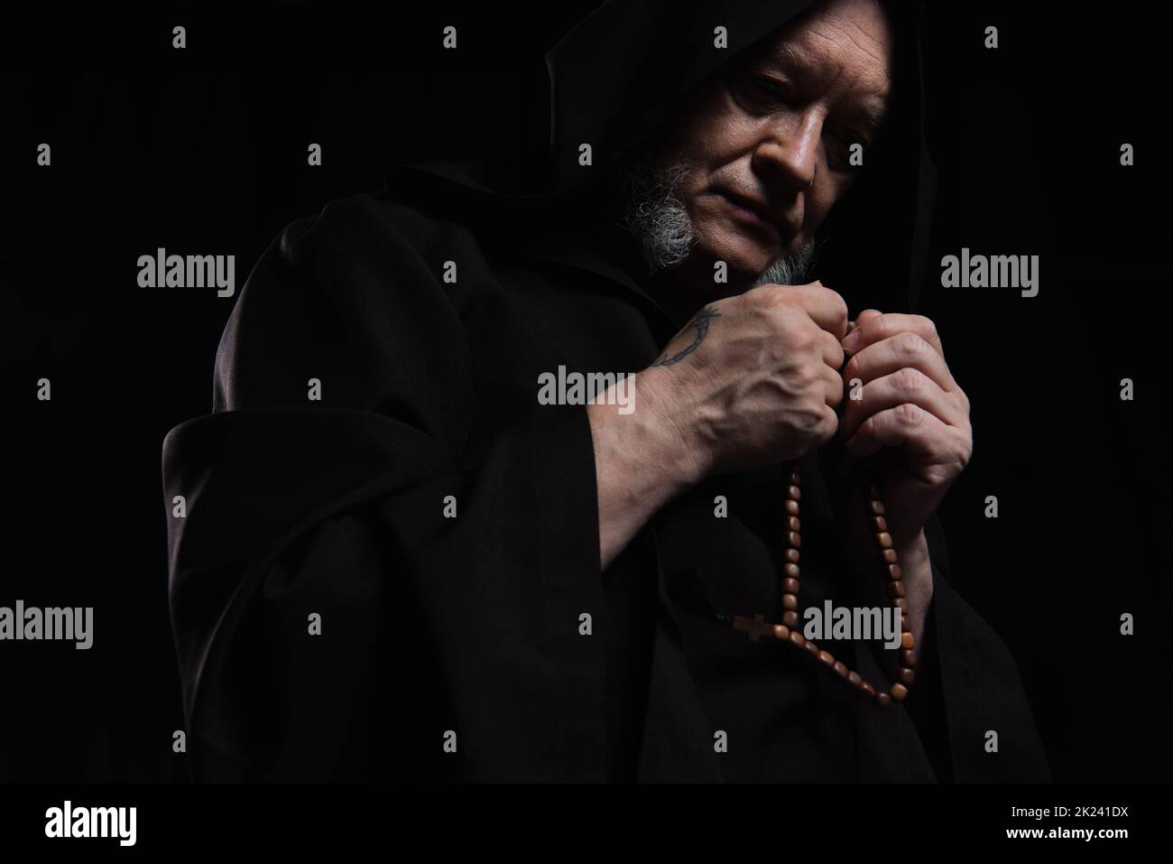 low angle view of monk in hooded robe praying with rosary isolated on ...