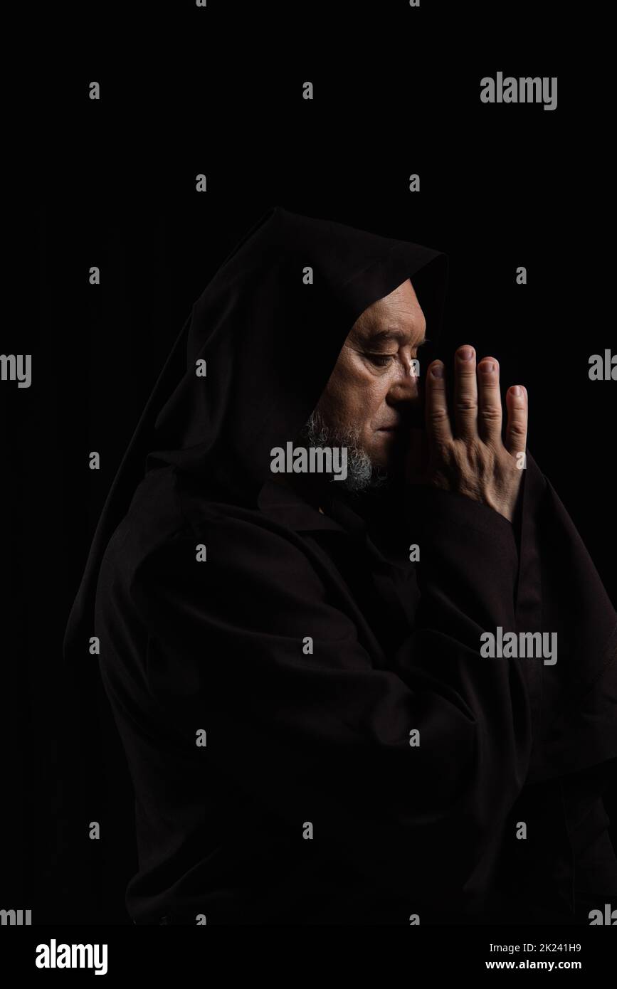 side view of medieval abbot in hood praying isolated on black,stock ...