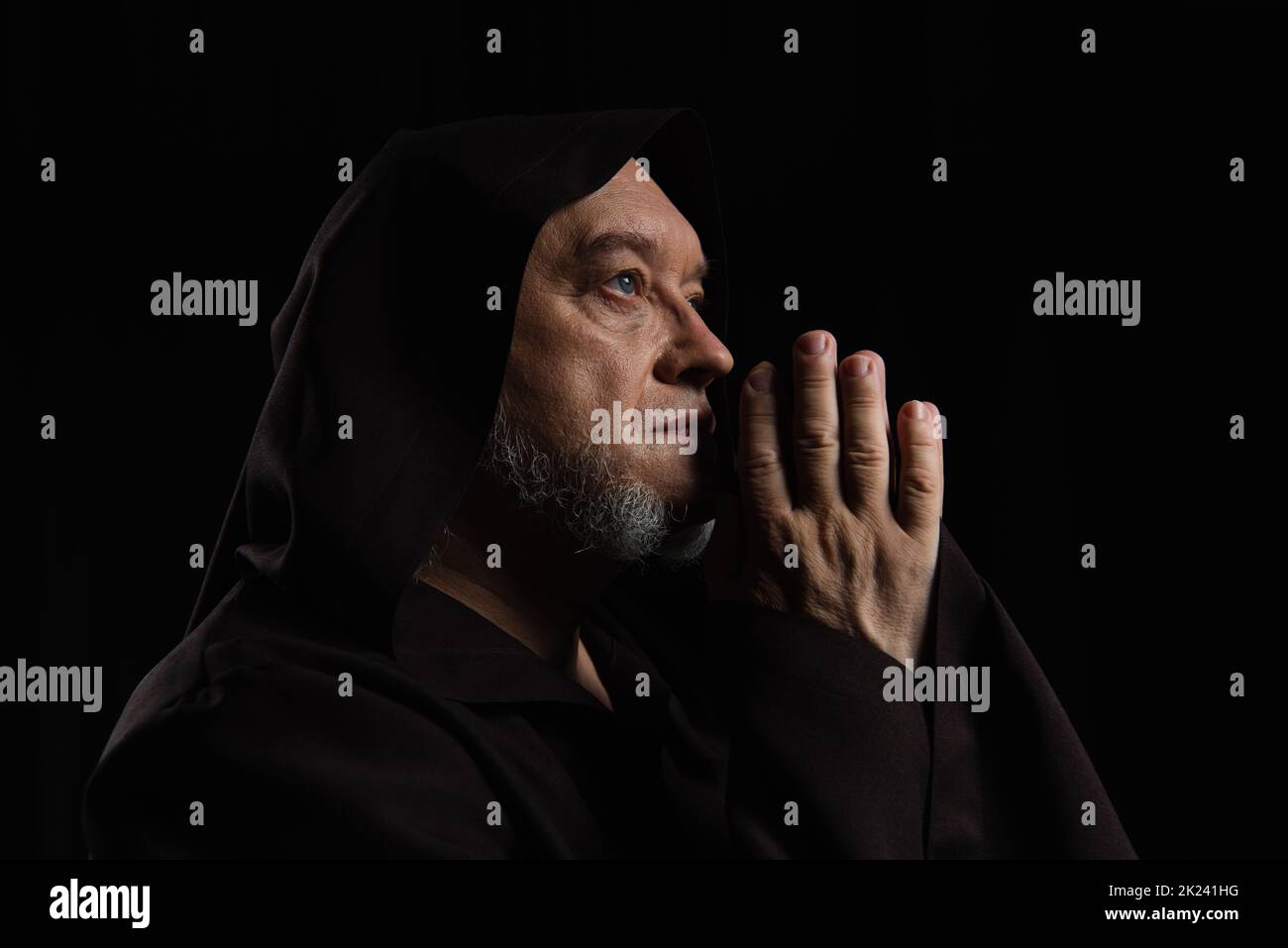 side view of medieval monk with praying hands near face isolated on ...