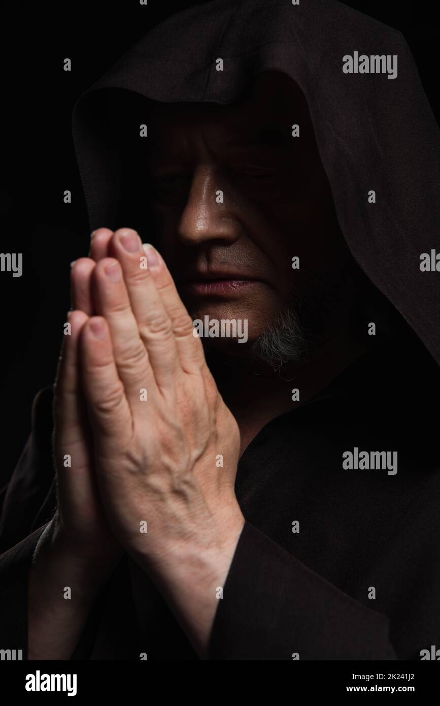 medieval monk with closed eyes and praying hands isolated on black ...