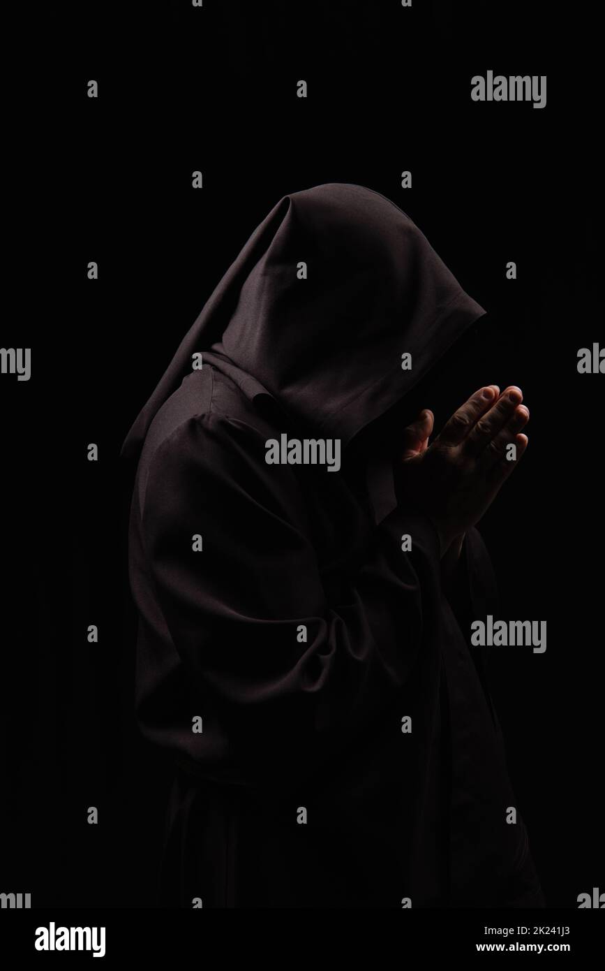 side view of mysterious monk in hood praying isolated on black,stock ...