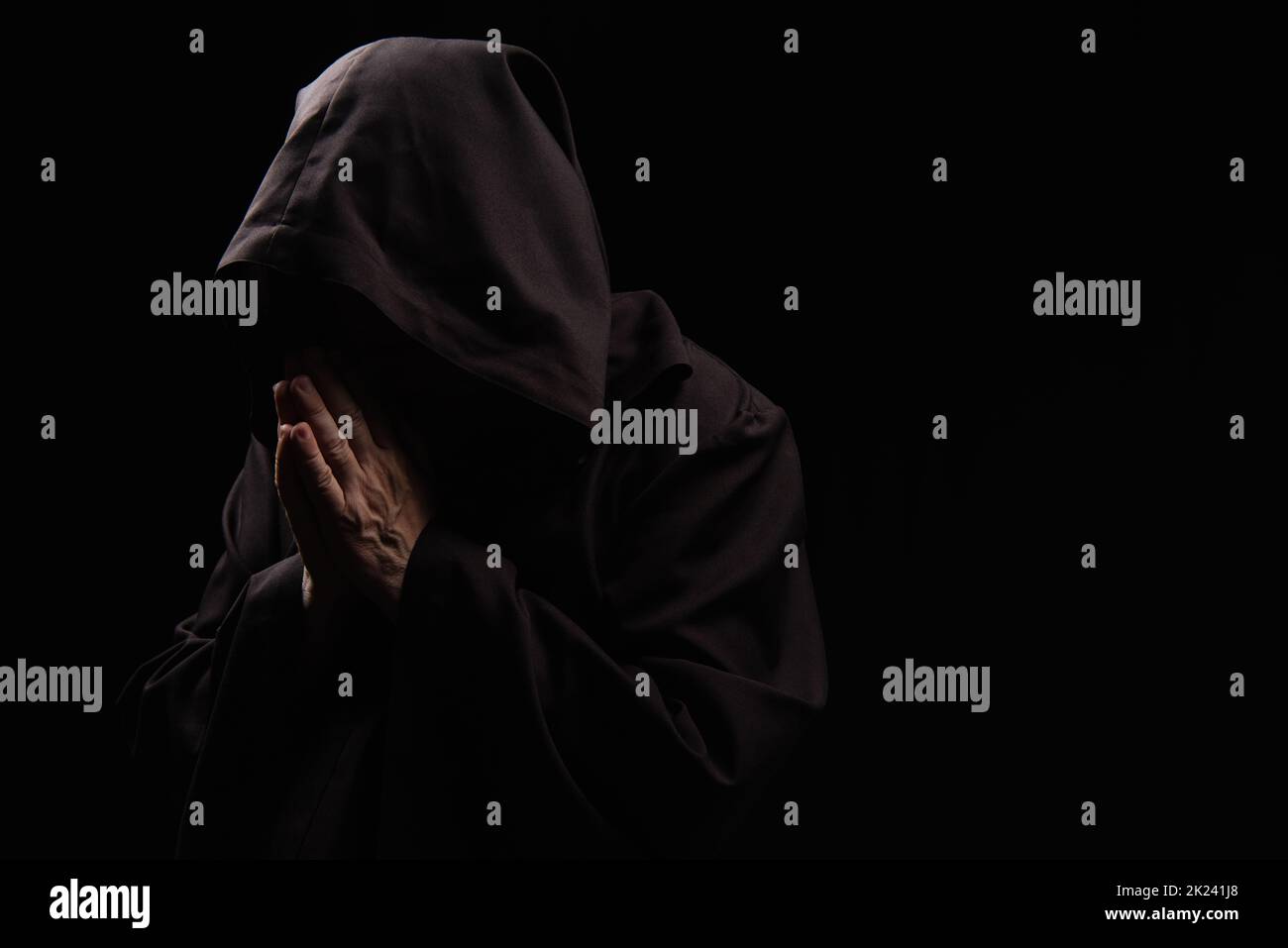 mysterious priest in hooded robe praying isolated on black,stock image ...