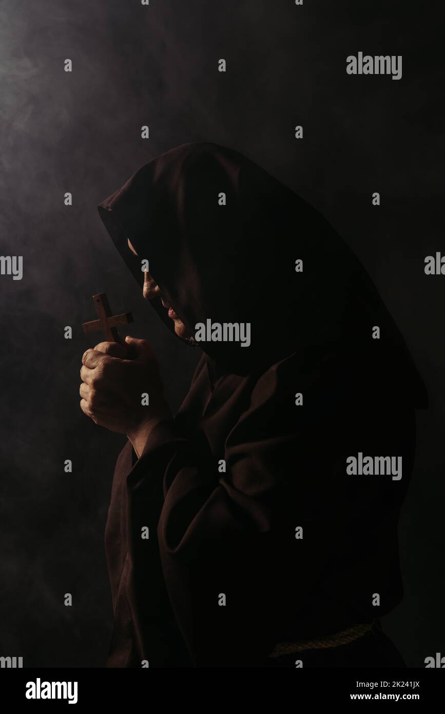 mysterious medieval monk in hooded robe praying with crucifix on black ...