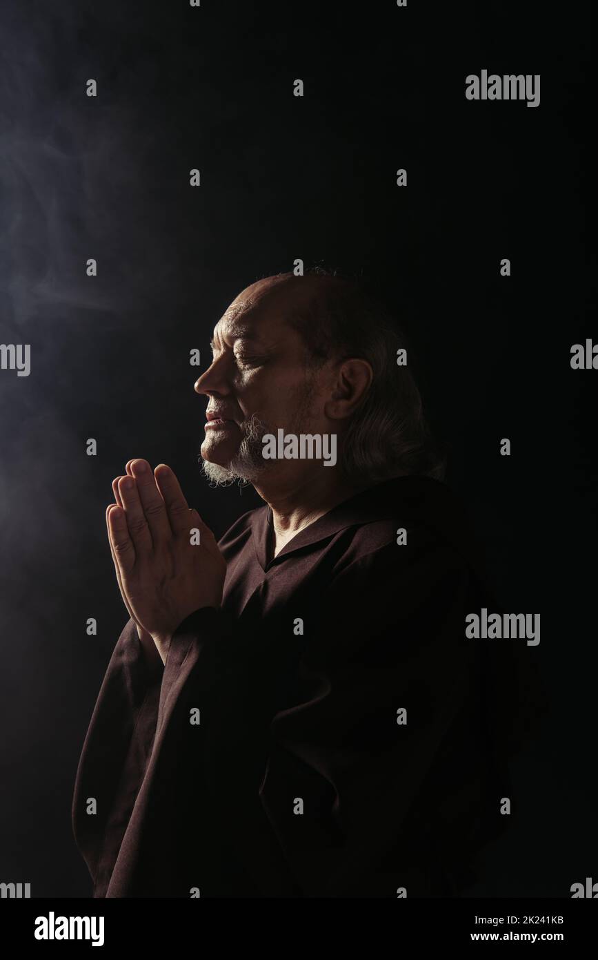 medieval priest with closed eyes praying at night on black background ...