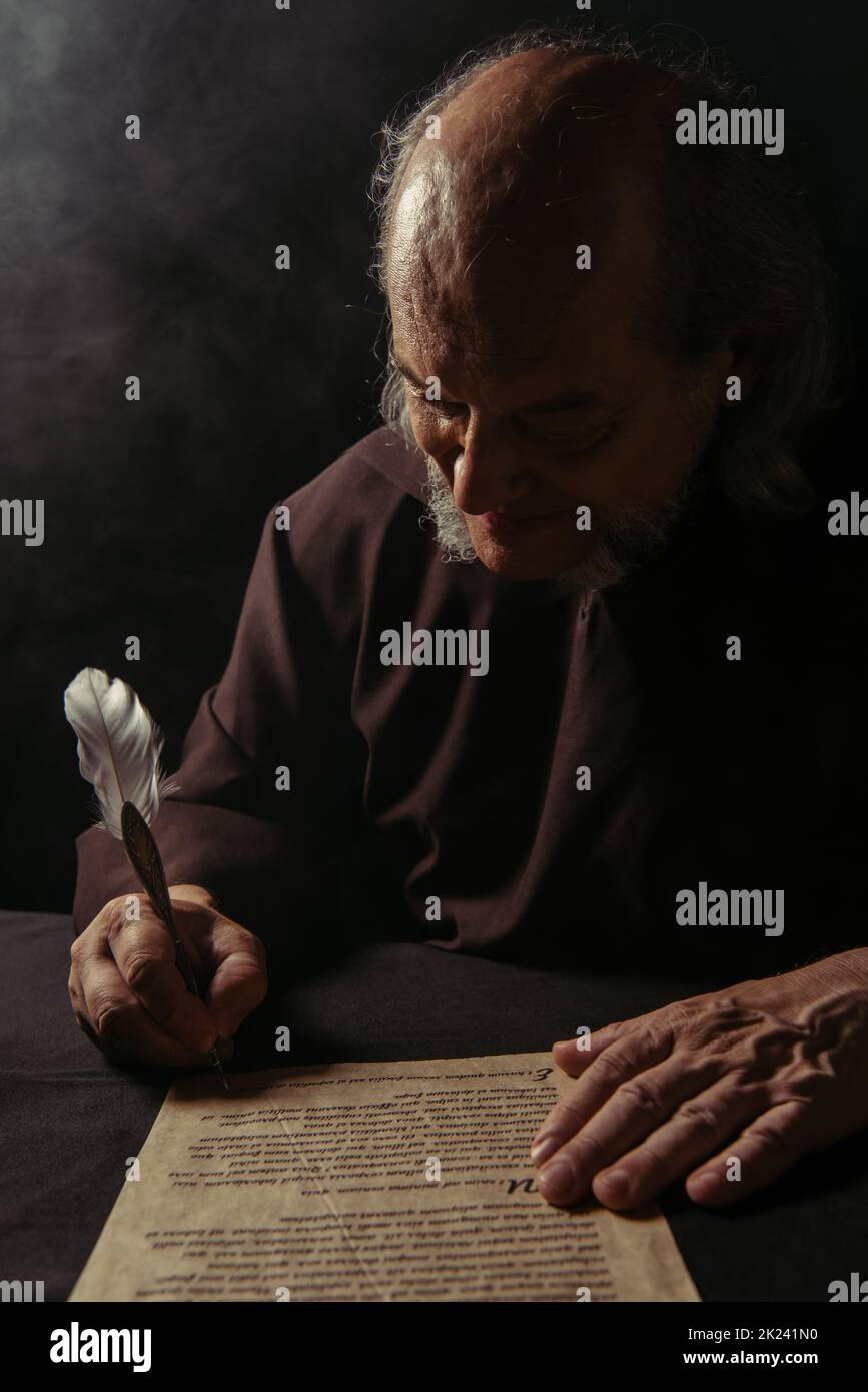 senior mysterious monk writing manuscript at night on black background ...