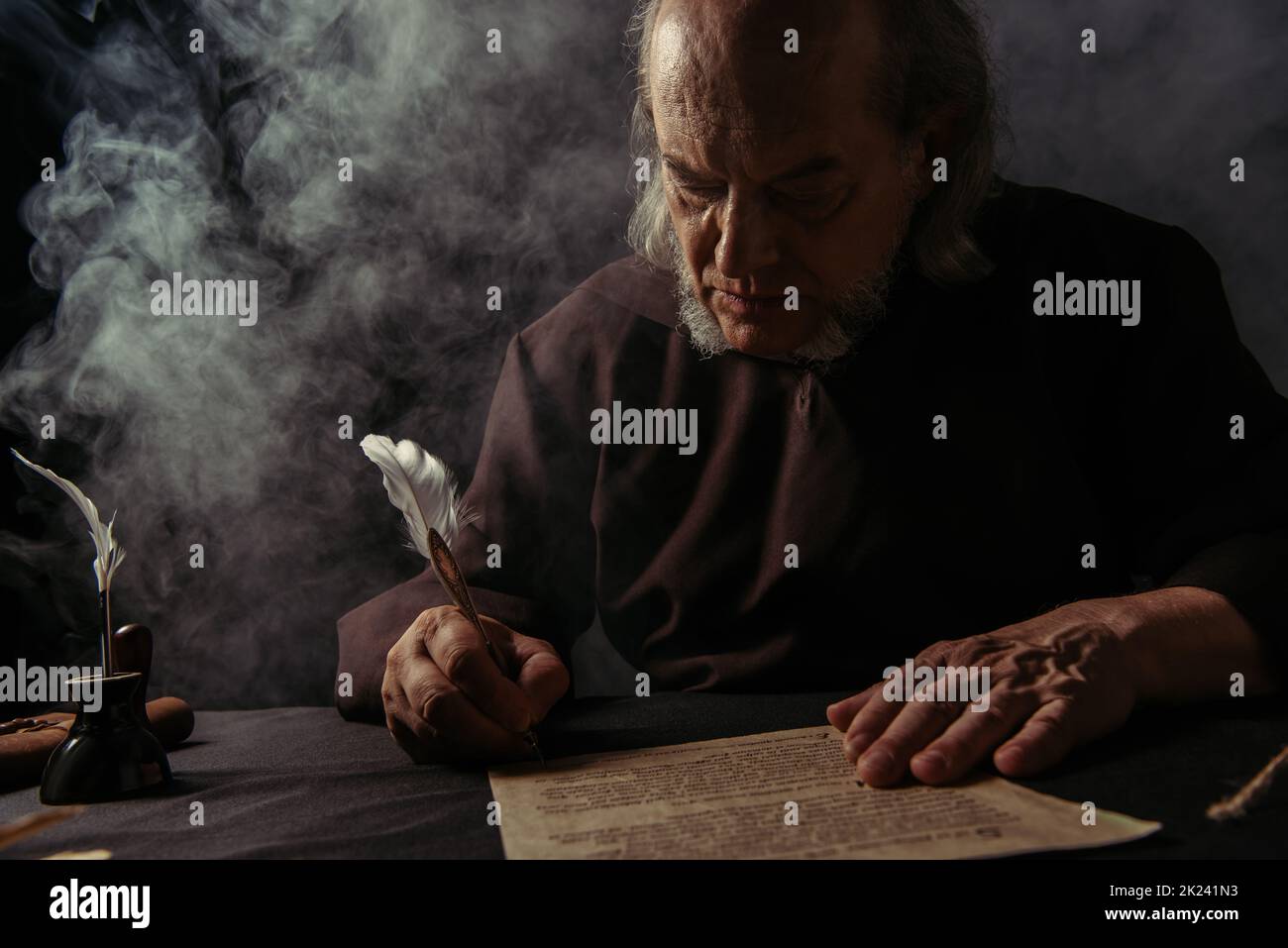 monk in black cassock writing manuscript on dark background with smoke ...