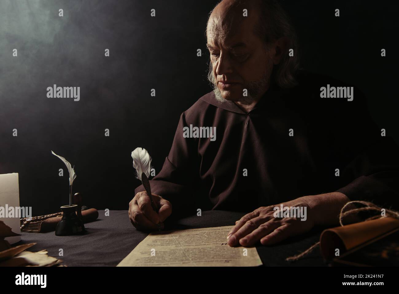 medieval priest in black robe writing manuscript on dark background ...
