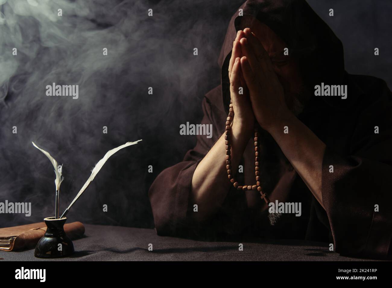 monk with rosary obscuring face with praying hands near inkpot and ...