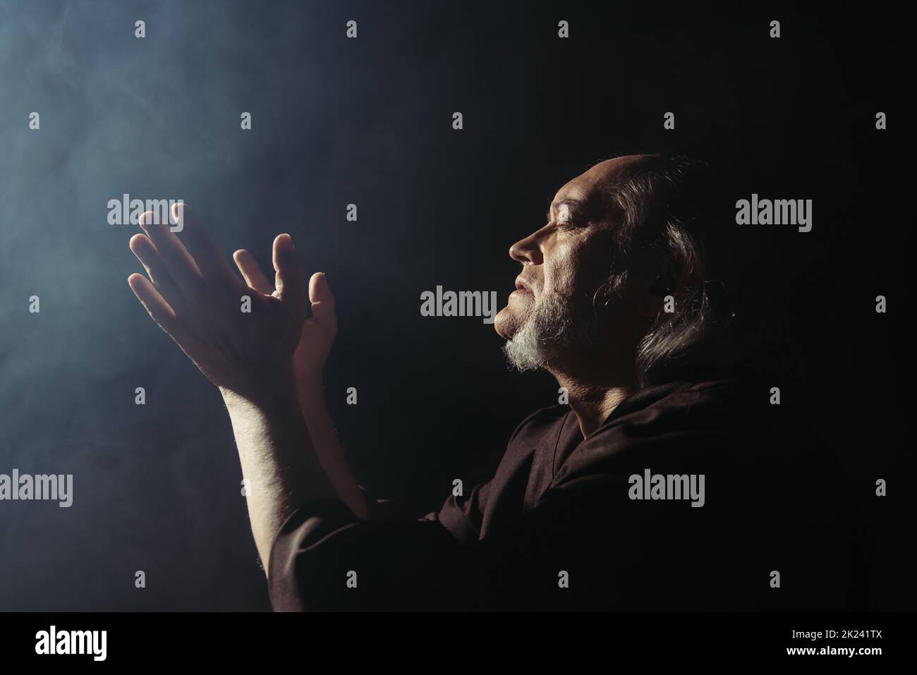 side view of medieval priest praying on black background with smoke ...