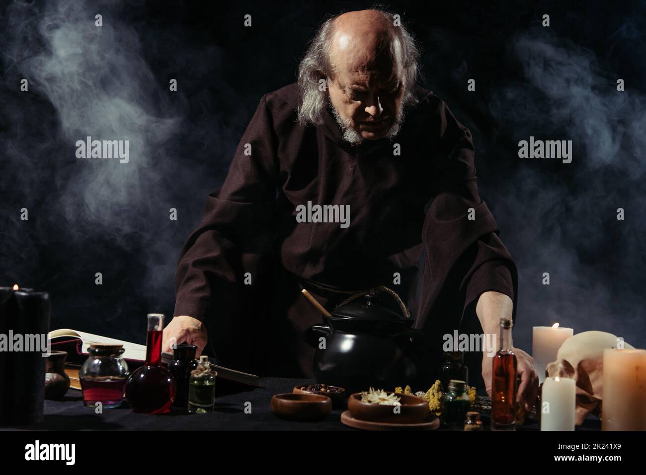 medieval alchemist preparing potion near liquid and dried ingredients ...
