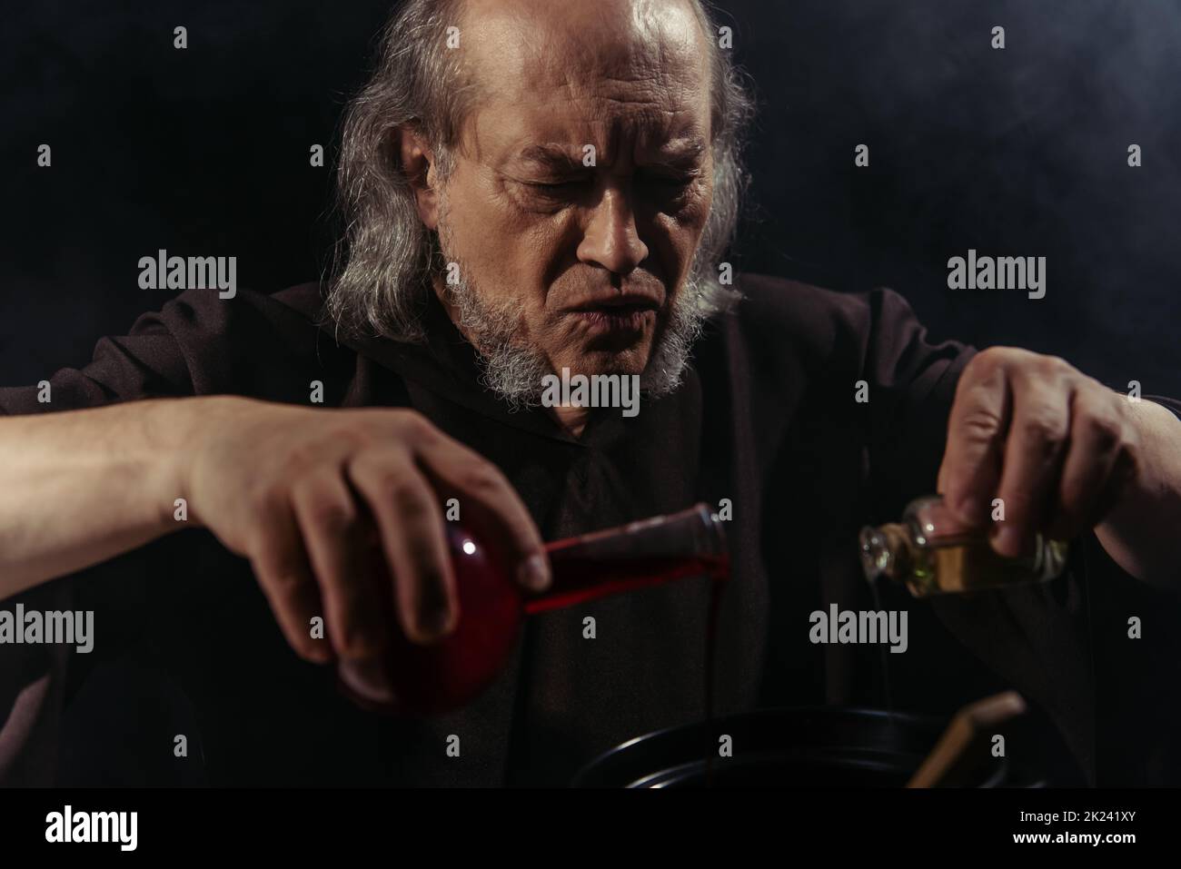 bearded alchemist mixing liquid ingredients and preparing magic potion ...