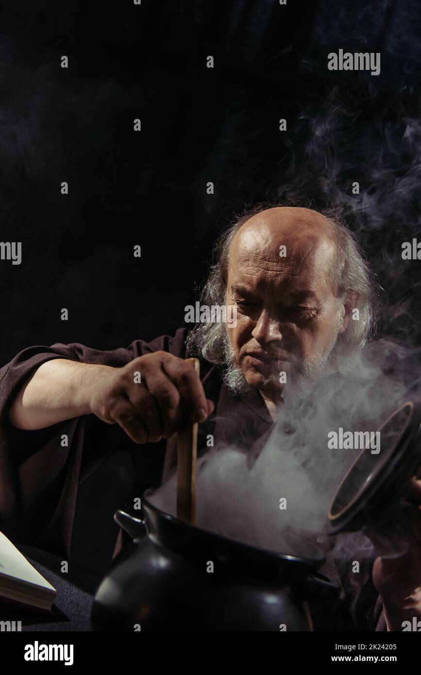 medieval healer preparing magic potion in boiling pot isolated on black ...