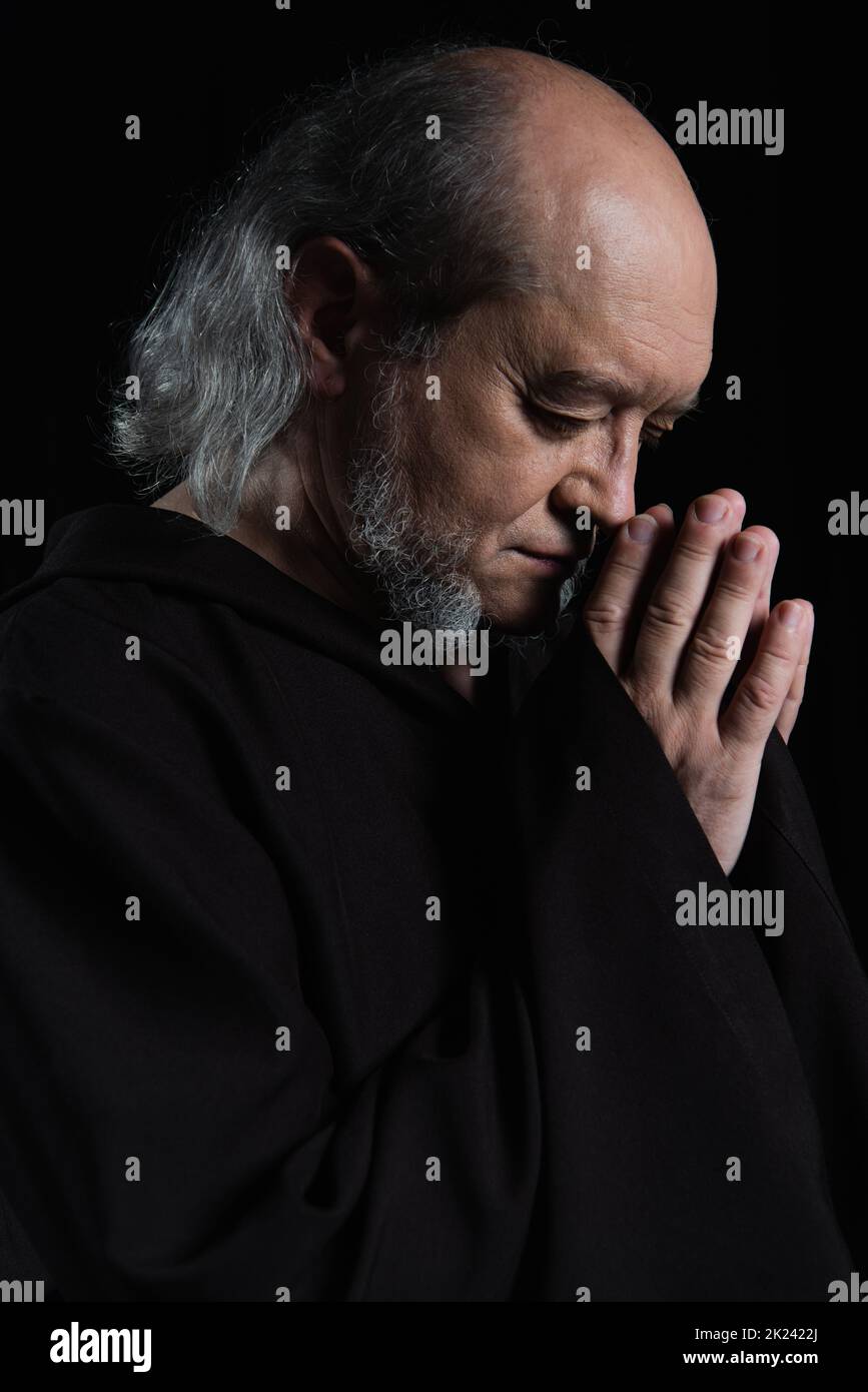 side view of senior medieval monk with praying hands near face isolated ...