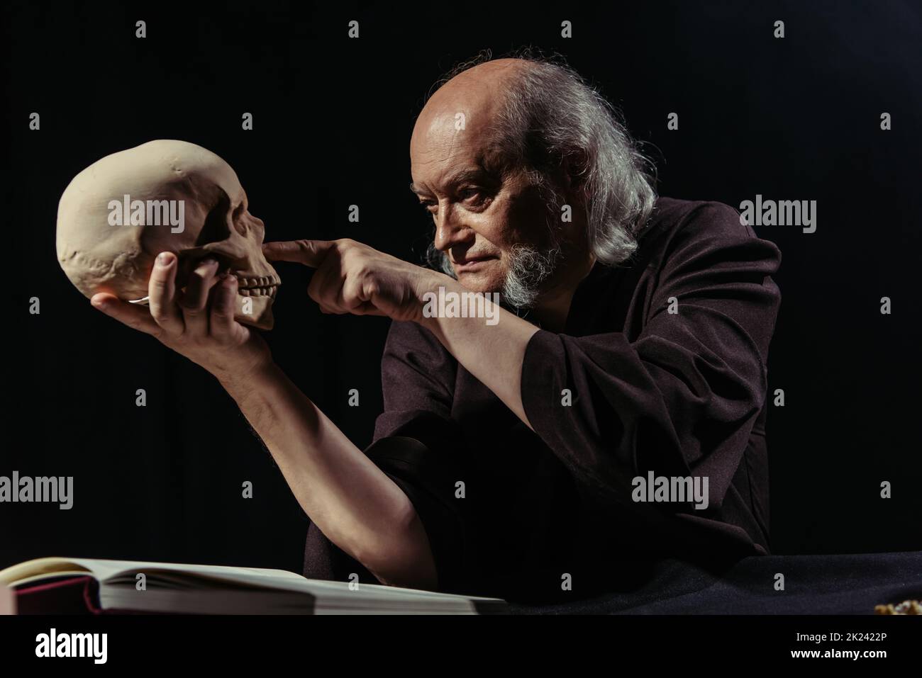 senior medieval philosopher pointing at human skull isolated on black ...