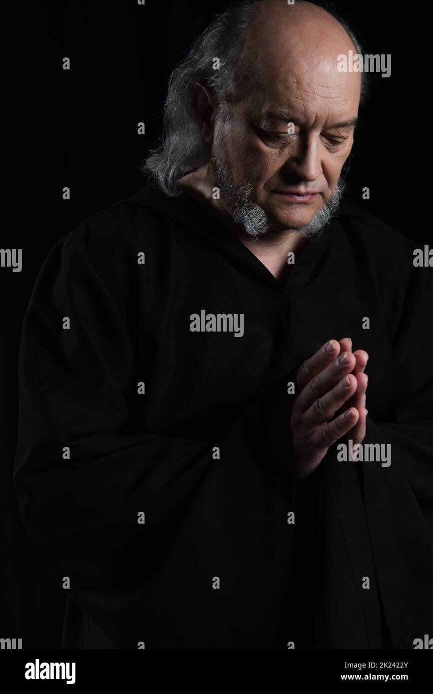 senior medieval monk in dark robe praying isolated on black,stock image ...