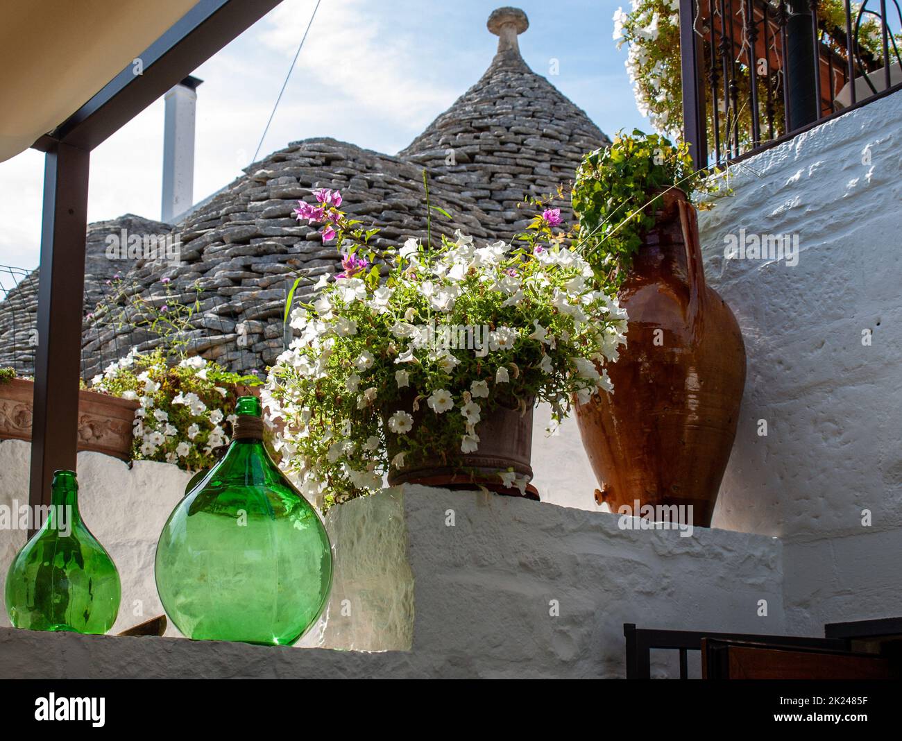 Demijohn, White petunias and ceramic jug at cafe in Trulli village in ...