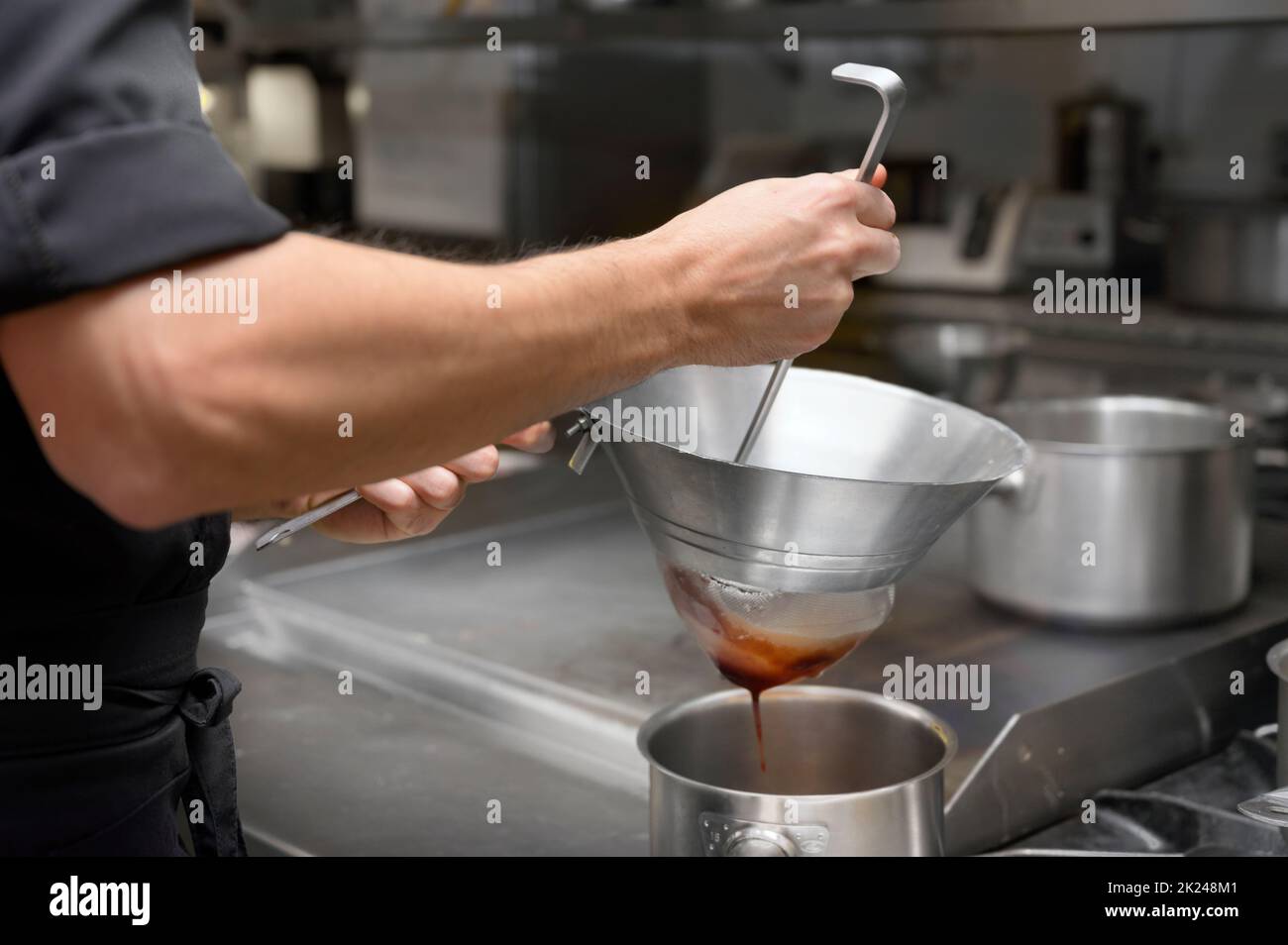 Cooking in the restaurant kitchen. Sifting sauce through a sieve. Chef ...