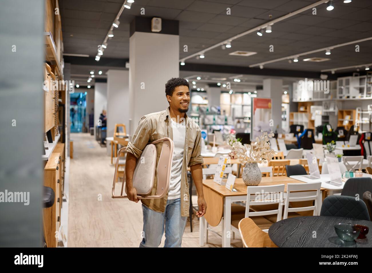 Man walking along store rack. Guy carrying folding chair in hand to ...