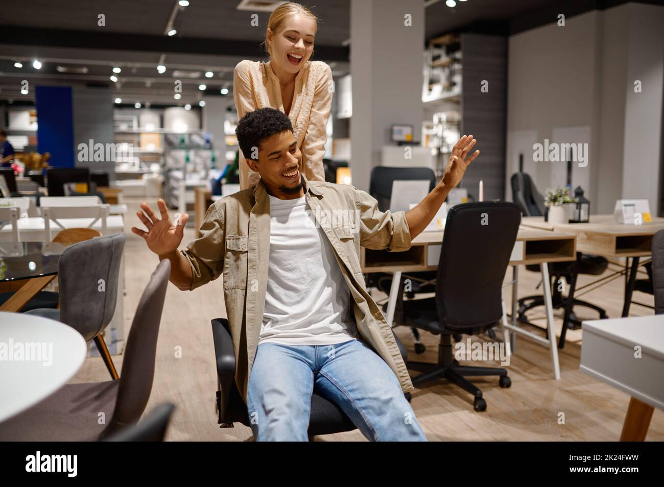Funny couple riding office chair at furniture shop. Man and woman of ...