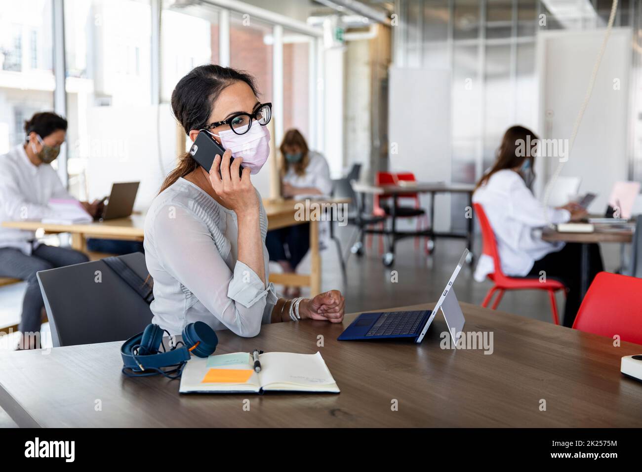 Woman in face mask using phone in socially distanced coworking space ...