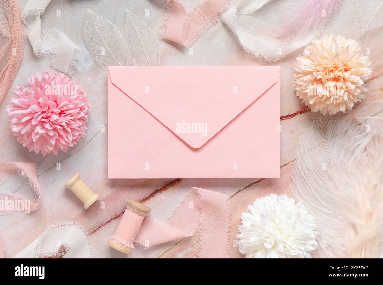 Pink envelope between pastel flowers, silk ribbons and feathers on ...
