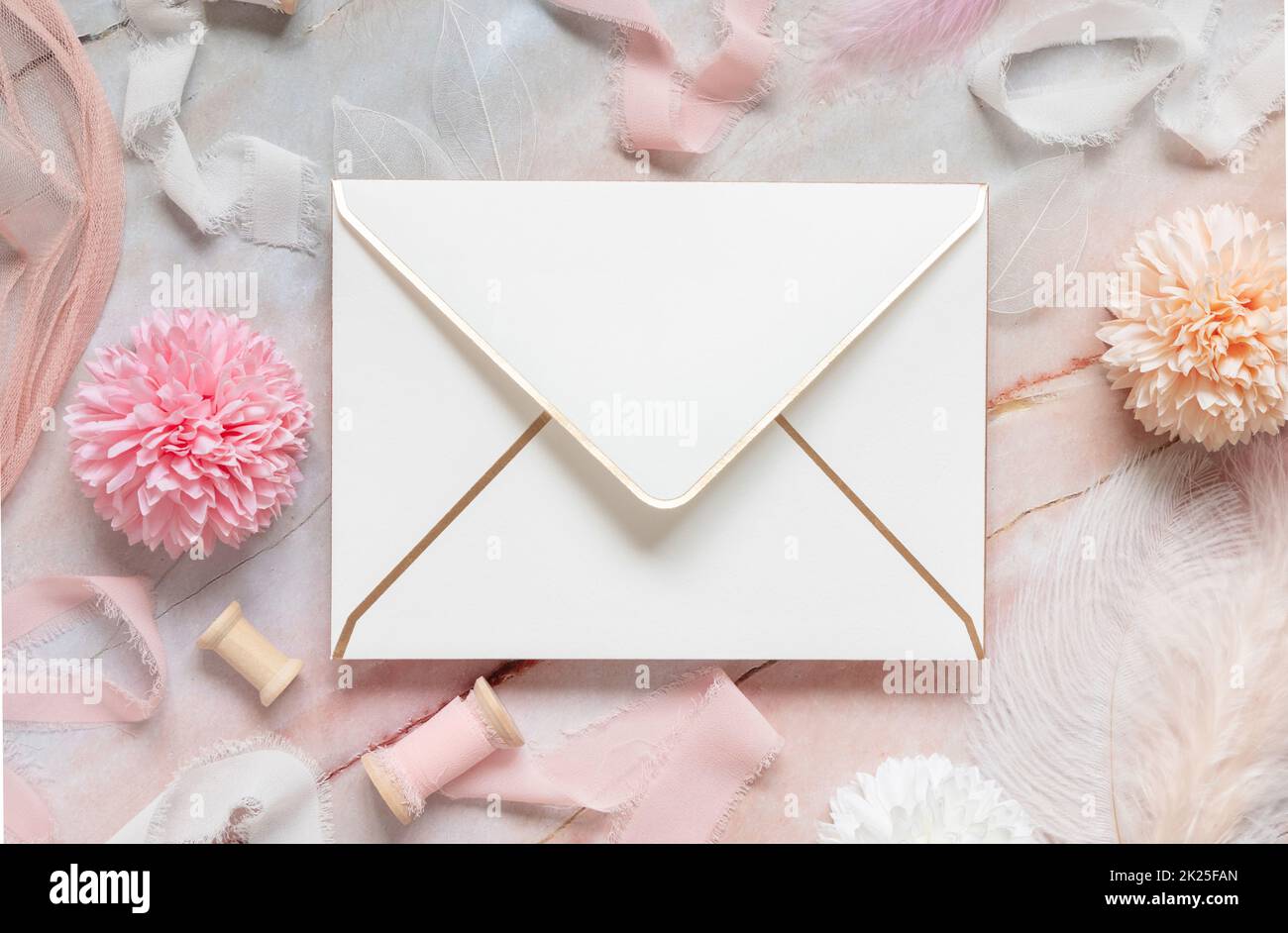 White envelope between pastel flowers, silk ribbons and feathers on ...