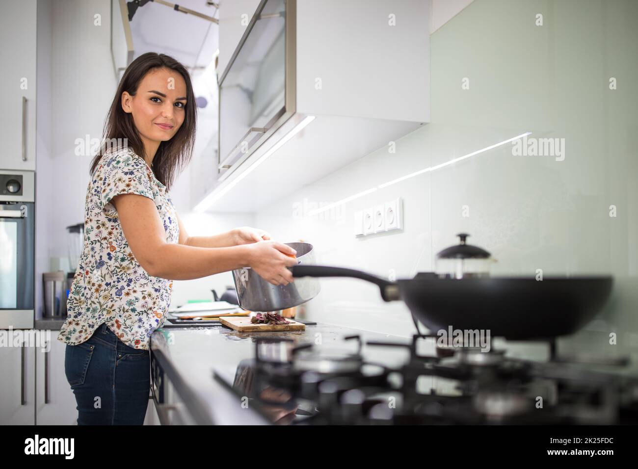 Pretty, young woman in her modern kitchen, by the fridge, about to cook ...