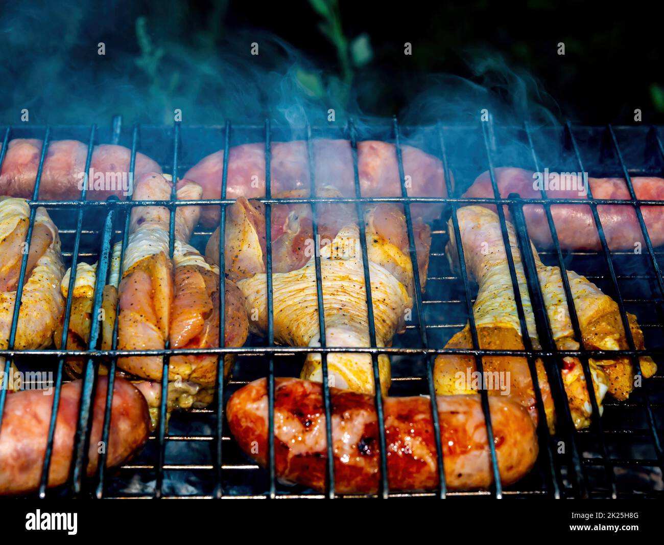 Chicken legs and meat sausages on an iron barbecue net over the fire Stock Photo - Alamy