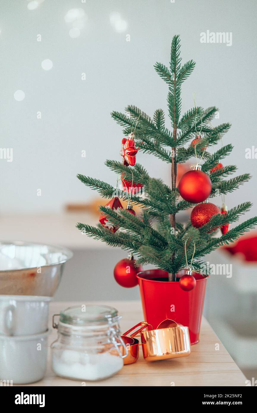 Decorated Christmas Tree in red pot placed on kitchen table near cups ...