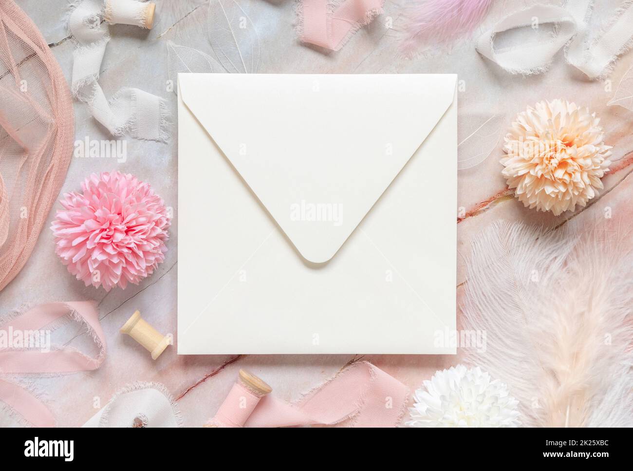 Square envelope between pastel flowers, silk ribbons and feathers on ...