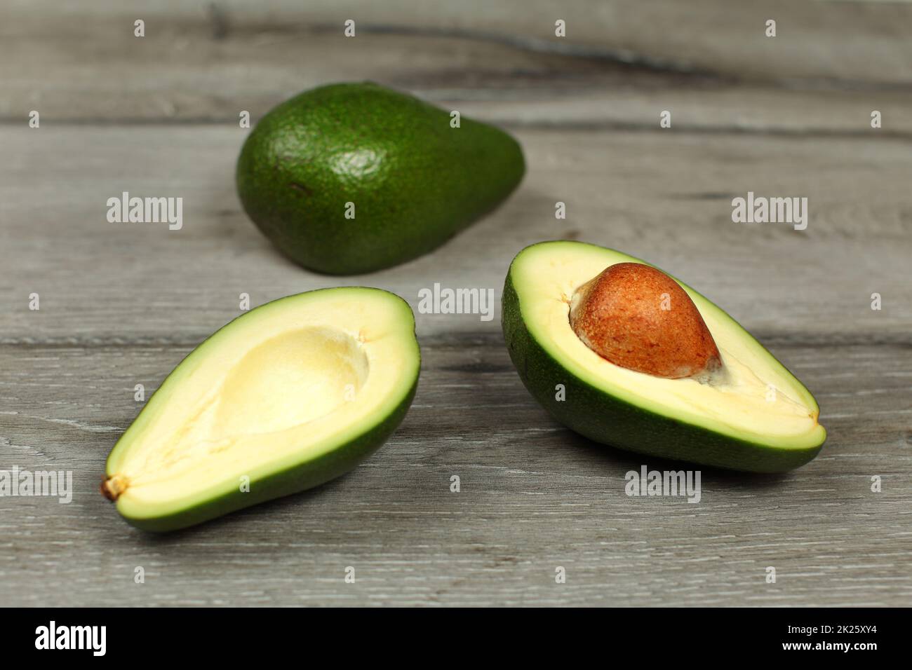 Two avocados, one cut in half, seed visible, on gray wood desk table ...
