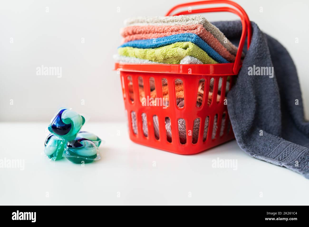 Multi-colored towels lie in a red laundry basket on a white background ...