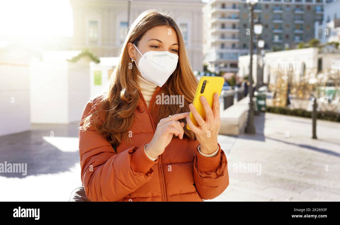 Woman in puffer jacket and medical face mask using her mobile phone ...