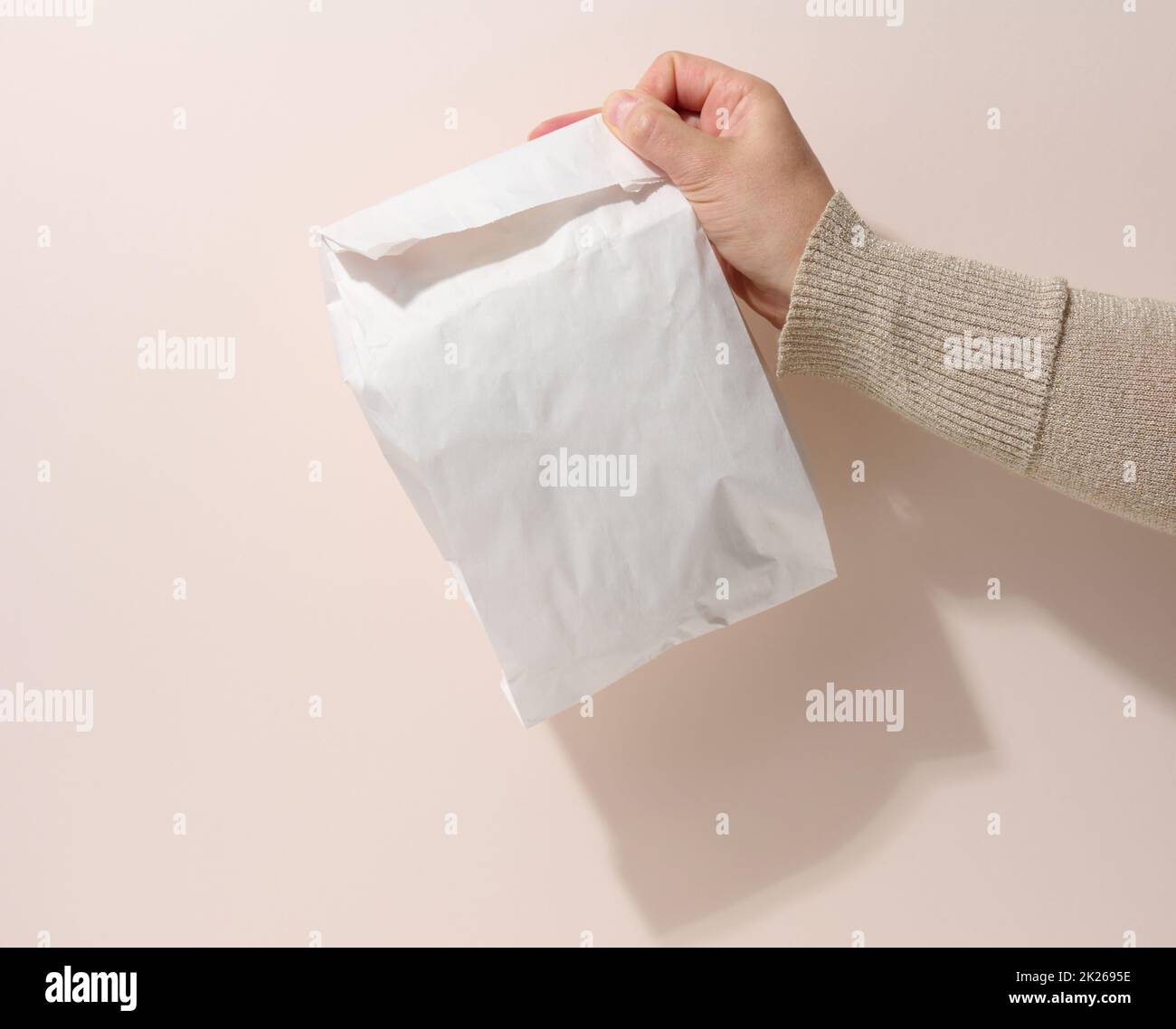 female hand holds a full paper bag on a beige background. Refusal from ...