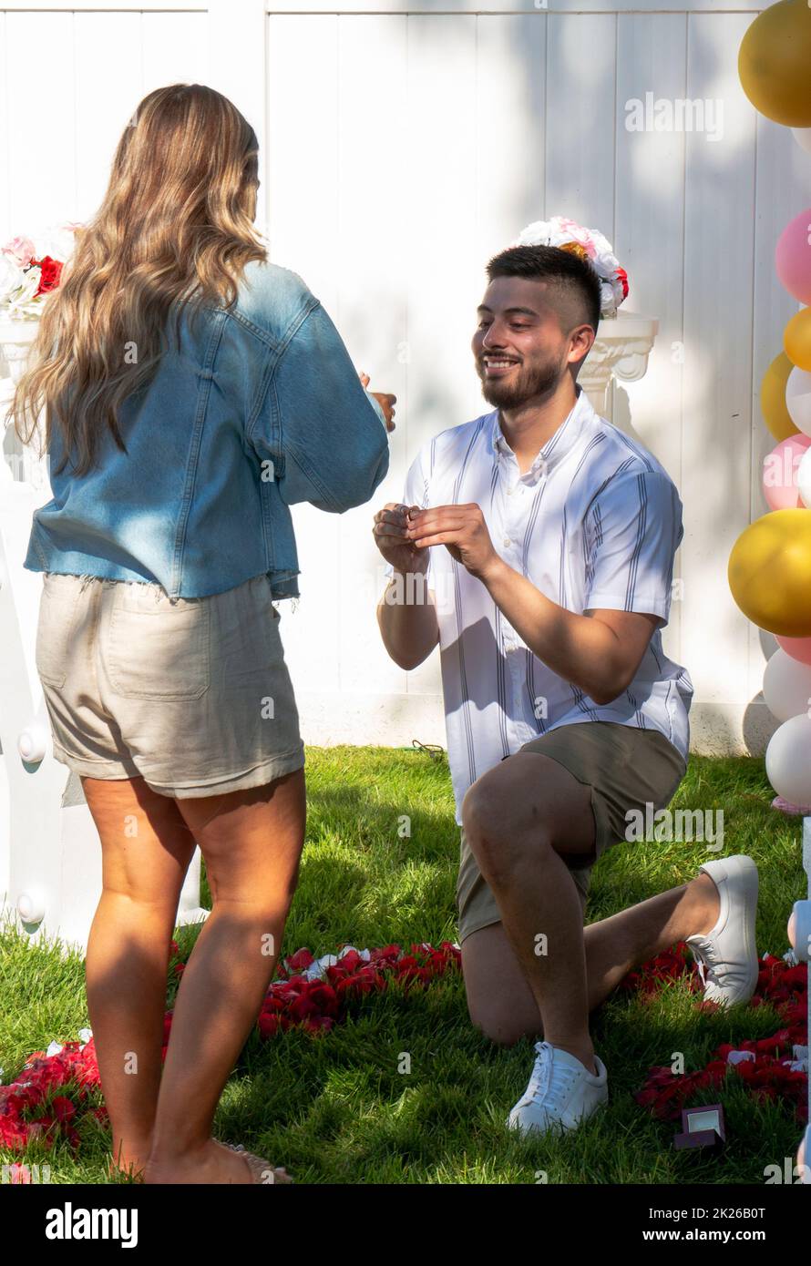 Man on one knee asking his girlfriend to marry him and placing the ring ...