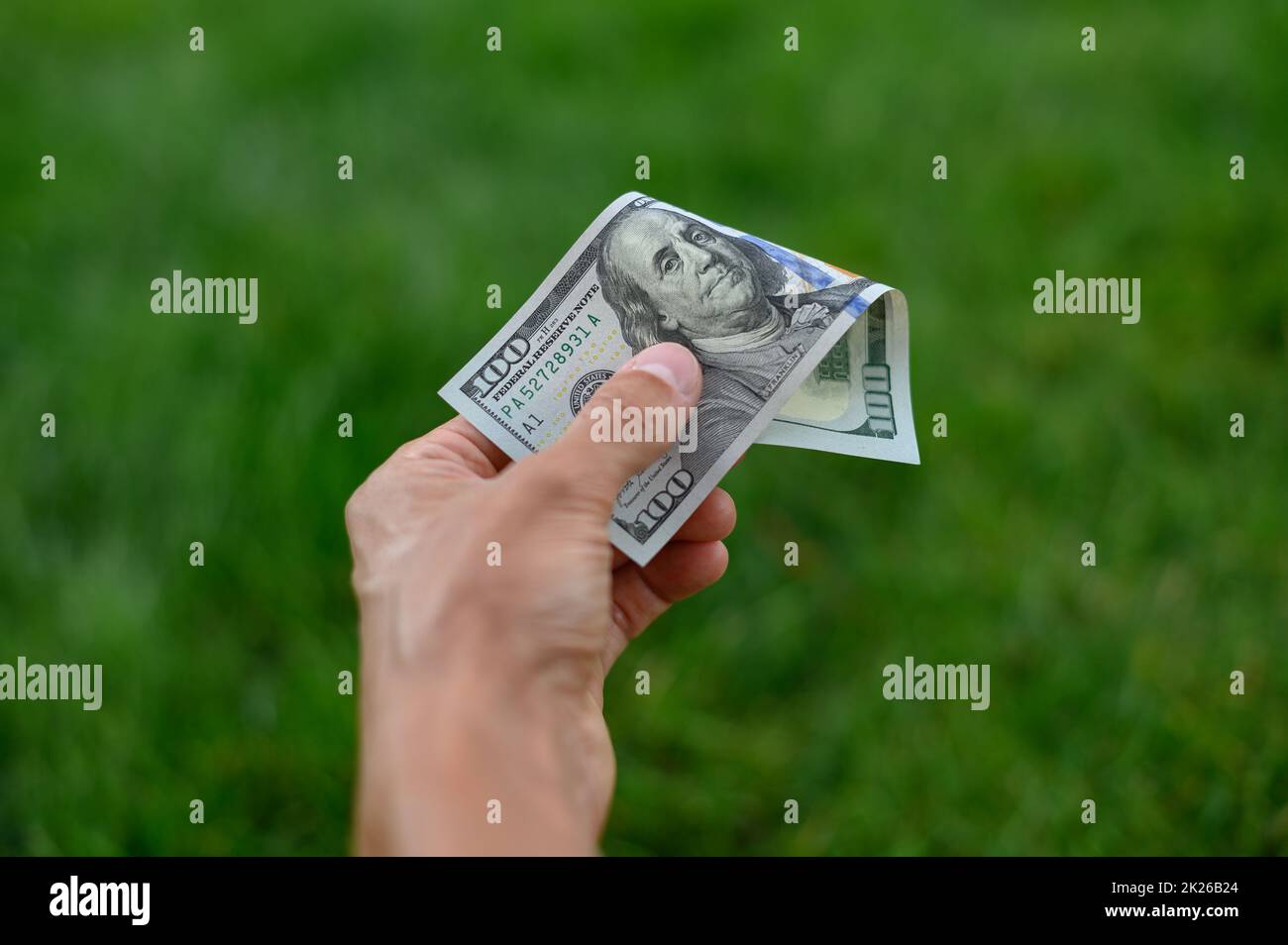 Close up 100 Dollar bank note in hand on grass background. One hundred ...