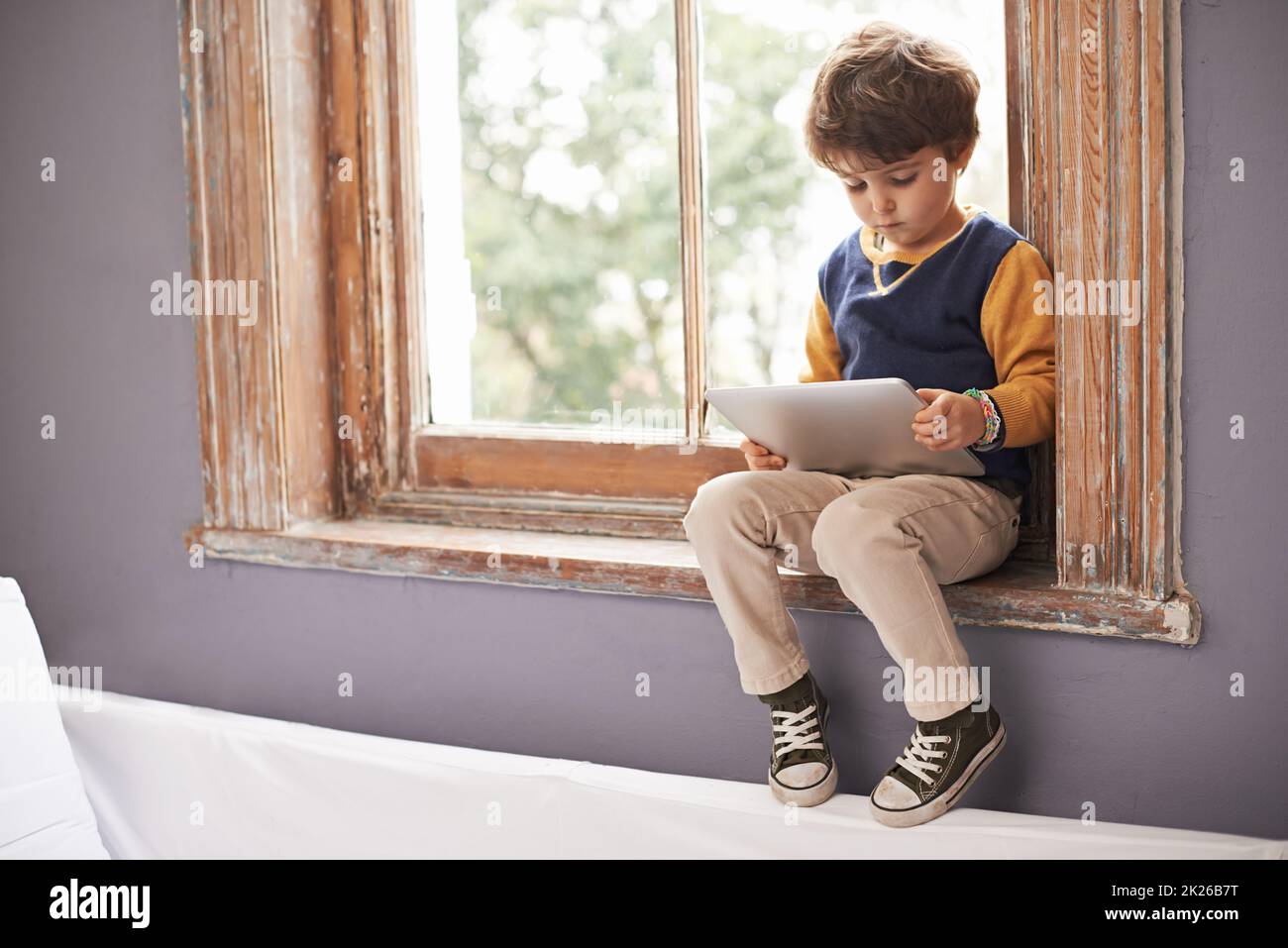 Hes tech savvy already. a cute little boy using a tablet while sitting ...