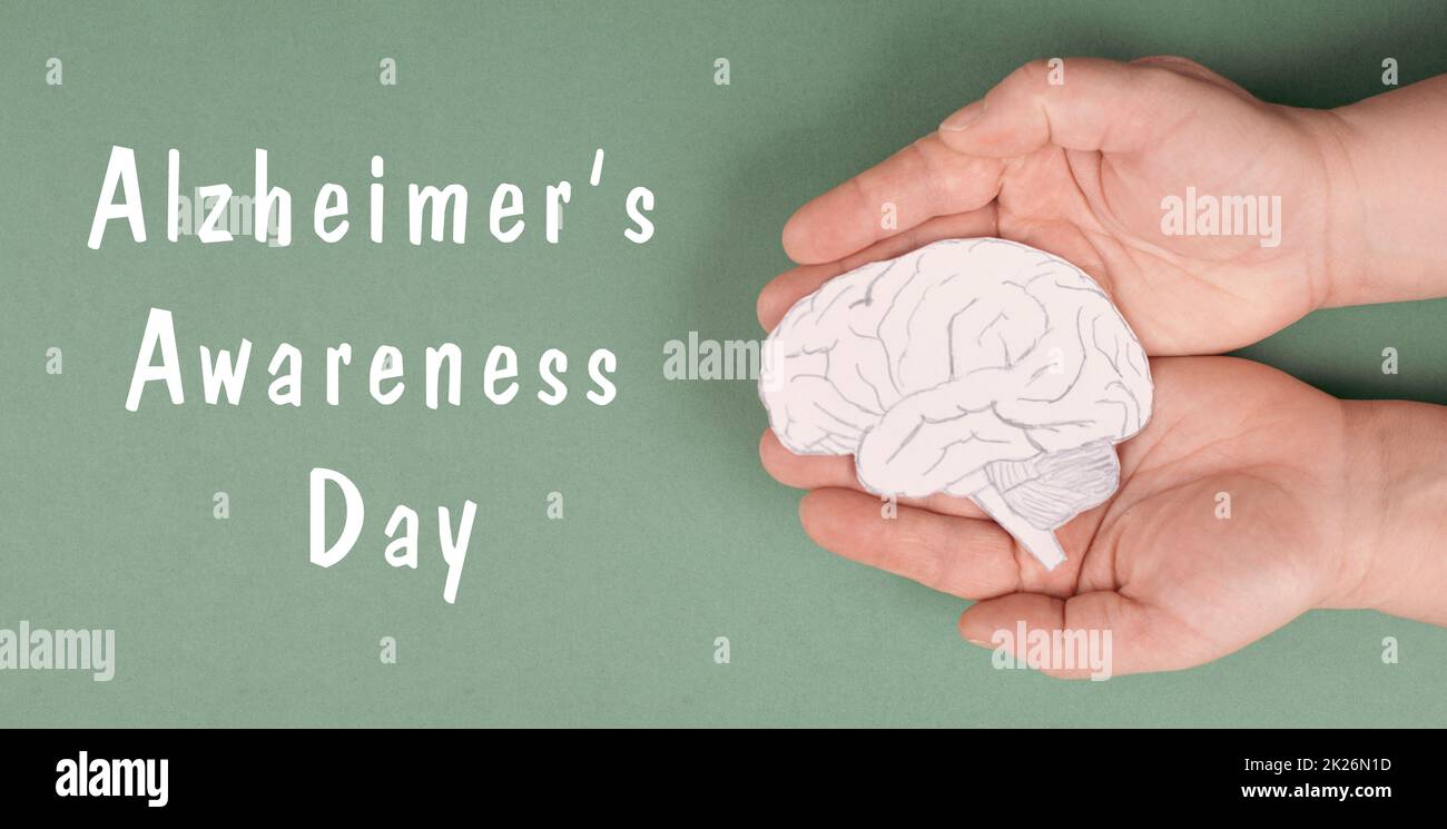 Alzheimer awareness day is standing on a paper, hands holding brain ...