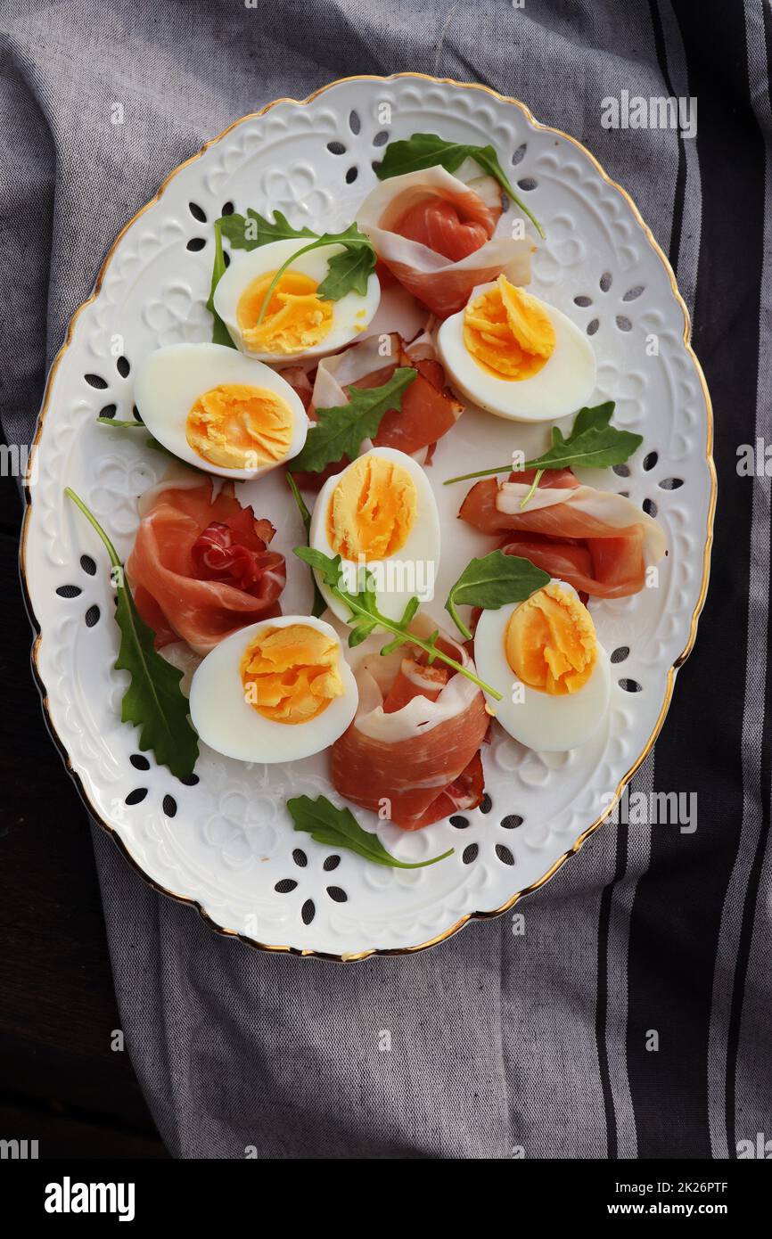 Italian salad. Boiled eggs with smoked ham and arugula on white plate ...