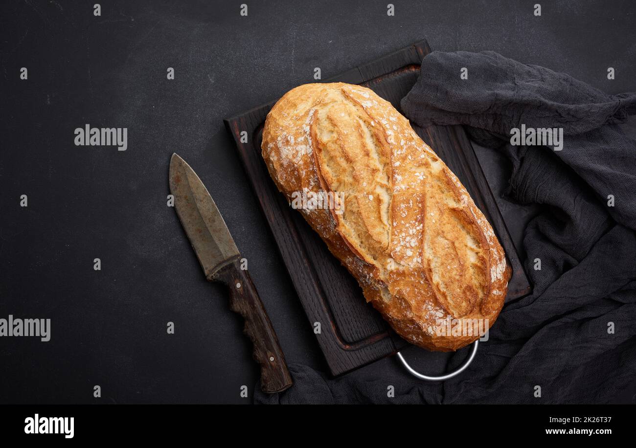 baked whole oval bread made from white wheat flour on a black table ...