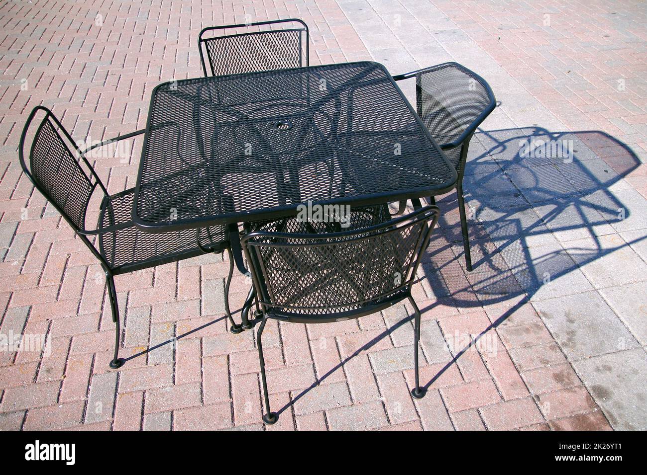 An outside iron table with four iron chairs with their shadow on a ...