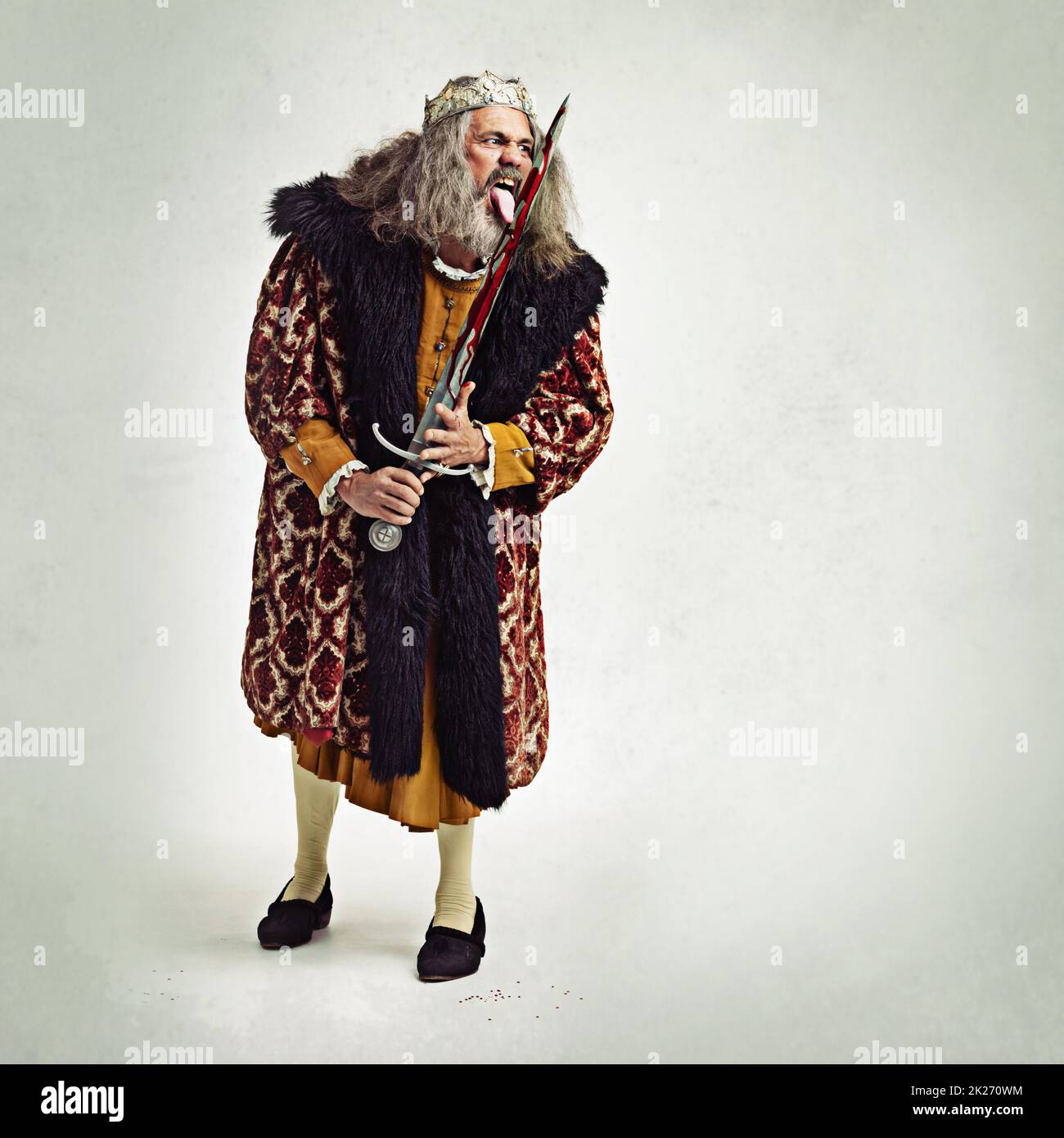 Ah The blood of my foes. Studio shot of a richly garbed king licking ...