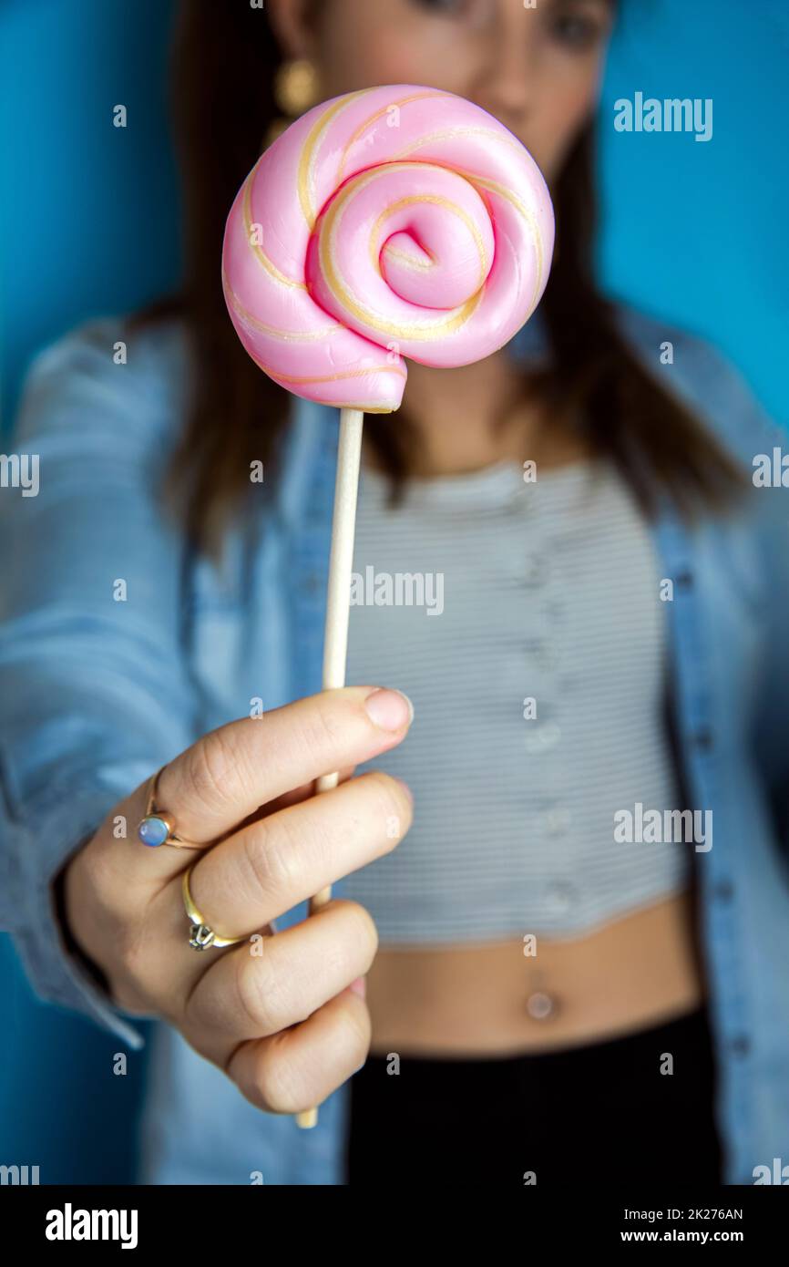 Happy beautiful woman giving colorful pink twirl lollipop on light blue ...