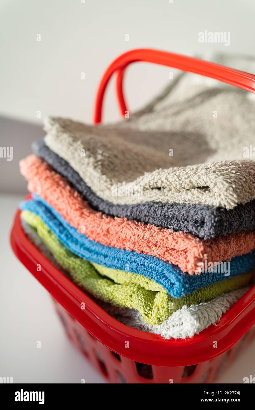 Multi-colored towels lie in a red laundry basket on a white background ...