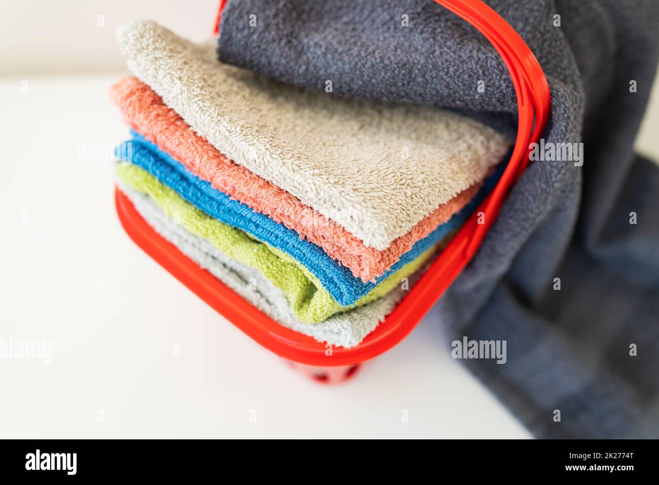 Multi-colored towels lie in a red laundry basket on a white background ...