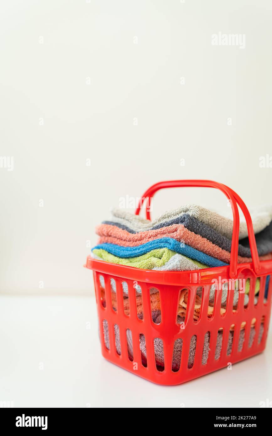 Multi-colored towels lie in a red laundry basket on a white background ...