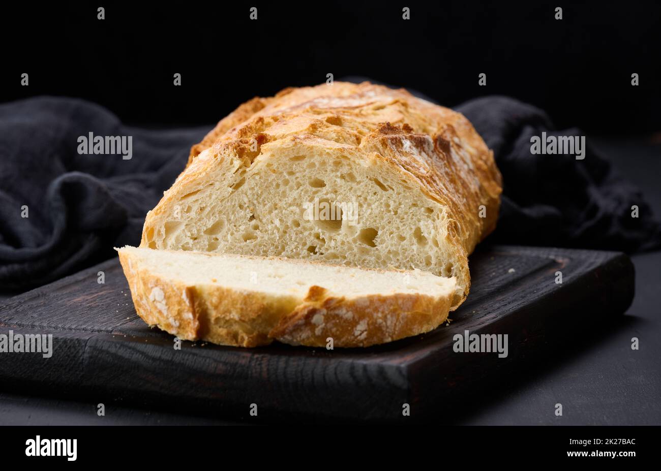 baked whole oval bread made from white wheat flour on a black table ...