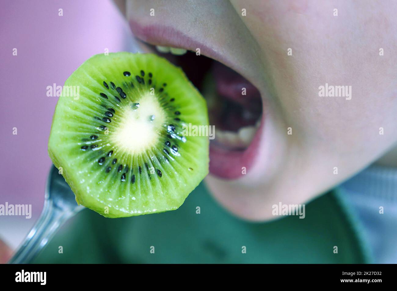 a child eating a kiwi with his mouth open, a slice of kiwi fruit stuck ...
