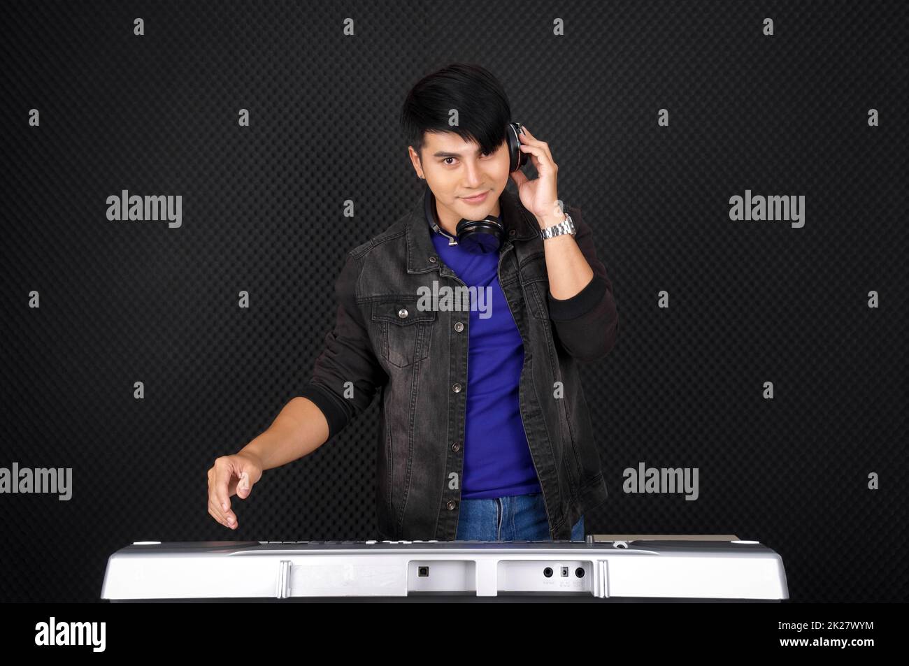 Young asian man with headphones playing an electric keyboard in front ...