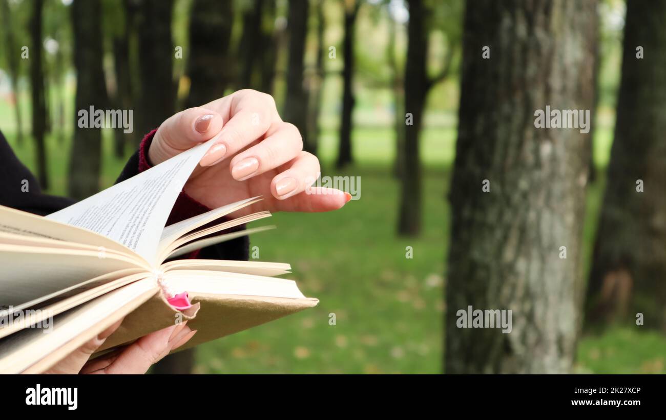 Girl reading a book in the park. Female hands flipping pages of paper ...